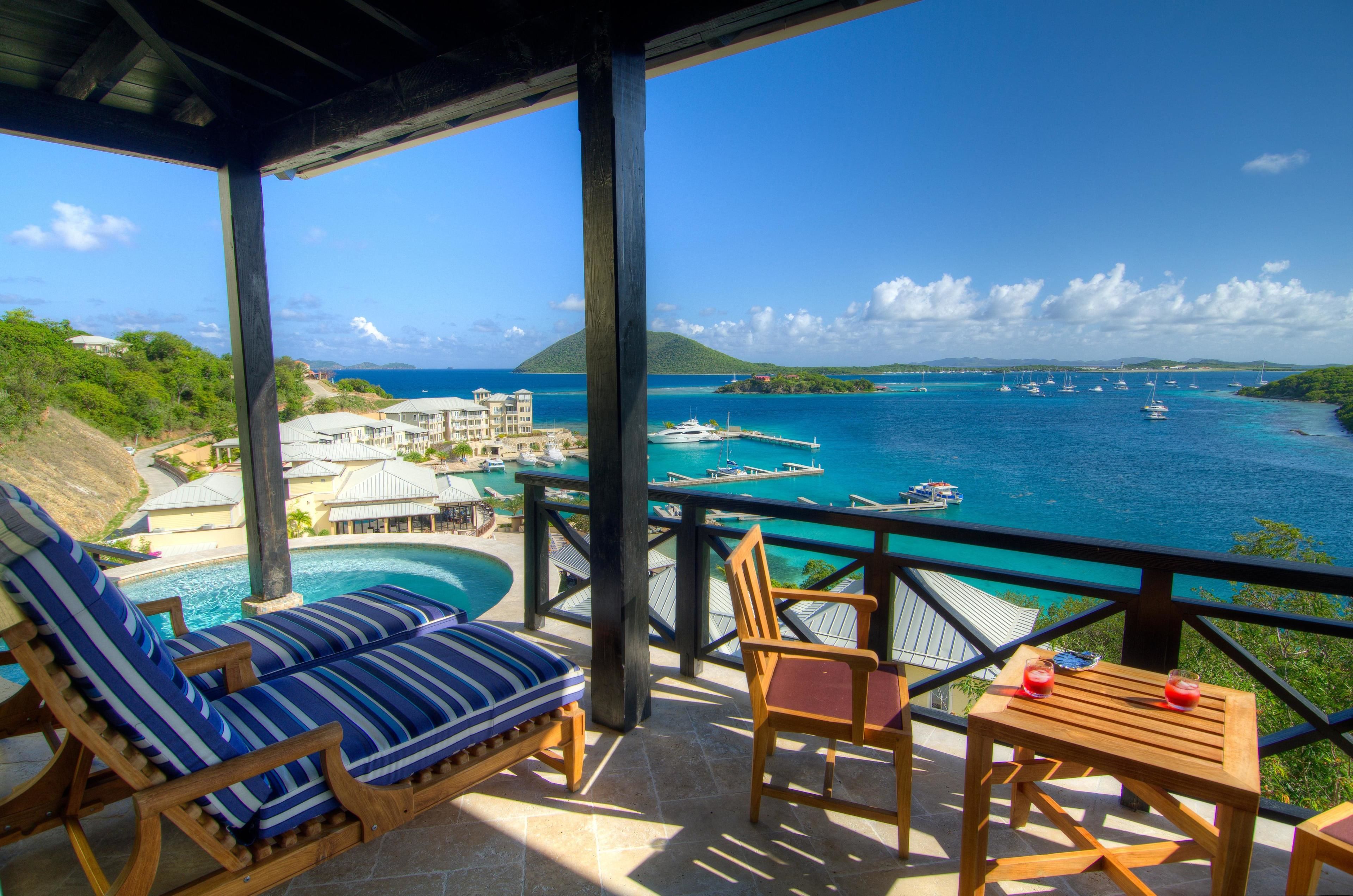 Uma varanda com vista para o mar, cadeiras de lounge, uma mesa de madeira e uma piscina.