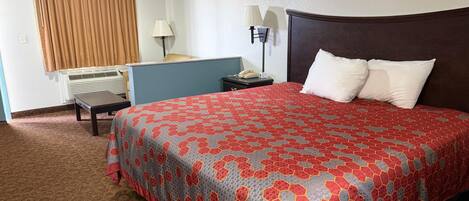 Quarto de hotel com uma cama grande, uma escrivaninha, uma cadeira, um abajur e uma janela com cortinas.