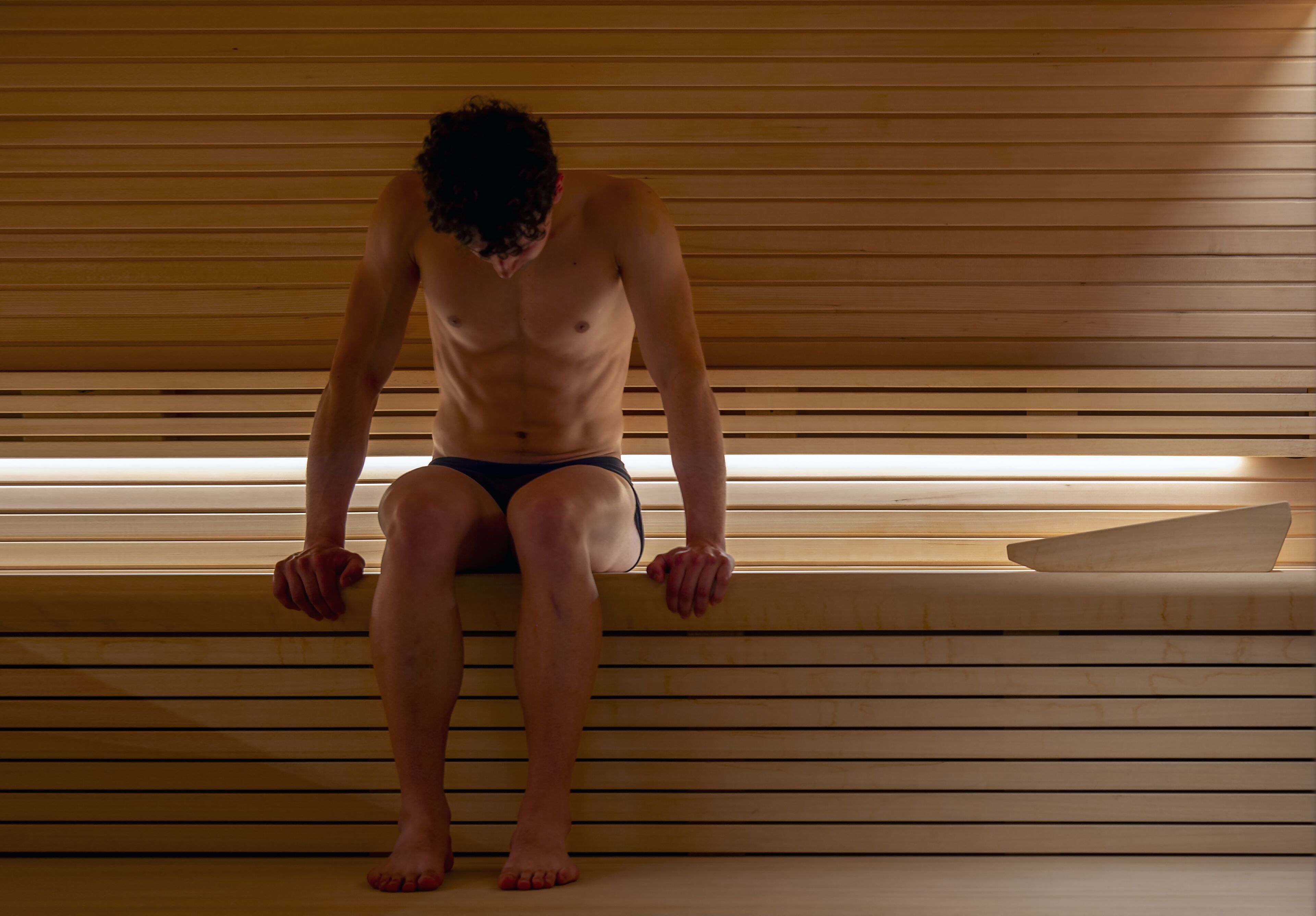 Uma pessoa sentada em um banco de madeira em uma sala de sauna.