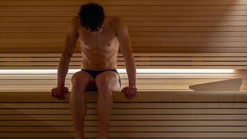 Uma pessoa sentada em um banco de madeira em uma sala de sauna.