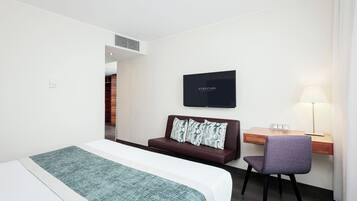 Quarto de hotel com uma cama, uma mesa com cadeira, uma televisão e uma luminária.