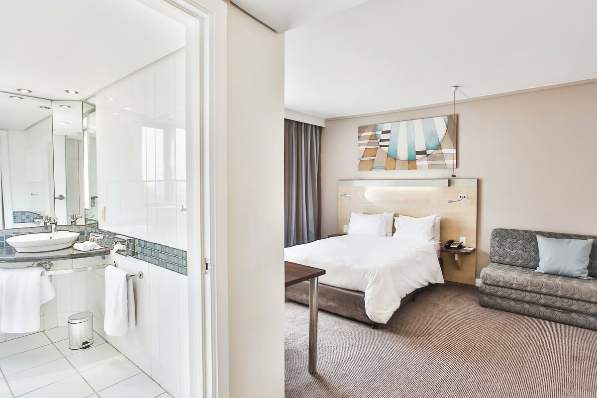 Quarto de hotel com banheiro, cama, sofá e um quadro na parede.