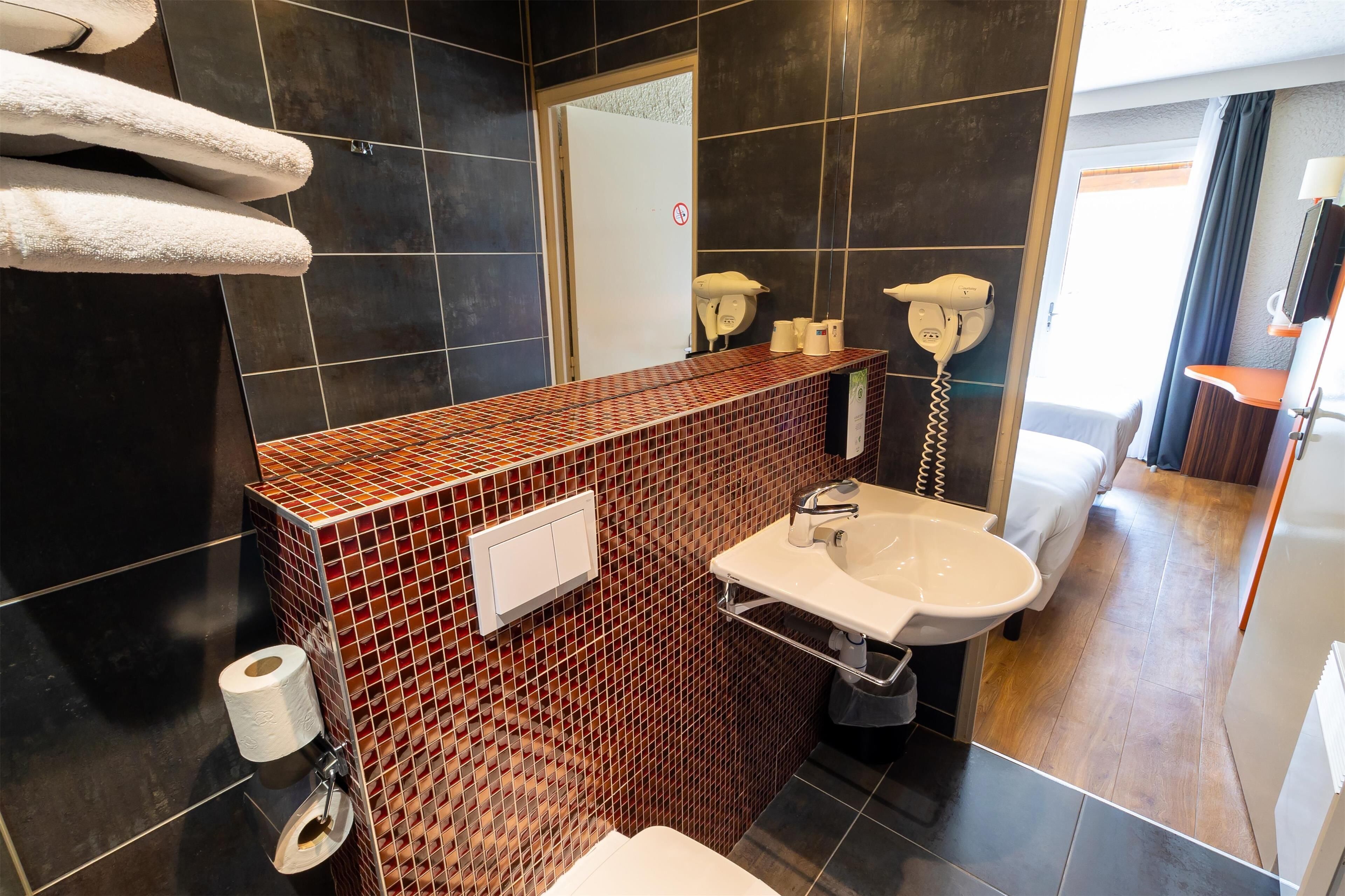 Um banheiro moderno com painel de azulejos, pia, espelho e porta-toalhas.