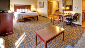 Quarto de hotel com cama, escrivaninha, cadeira, televisão e porta do banheiro.