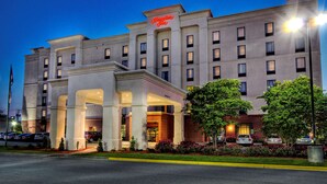 Um hotel grande, com vários andares e uma entrada destacada, com uma placa indicando "Hampton Inn".