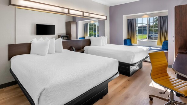 Quarto de hotel com duas camas, uma escrivaninha, uma cadeira, uma televisão e uma janela com cortinas.