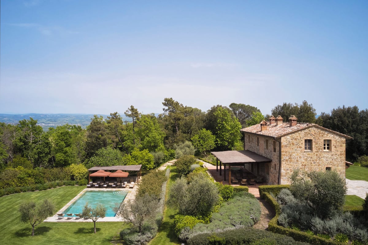 Uma vila de pedra com piscina, rodeada por vegetação exuberante e vista desobstruída da paisagem.