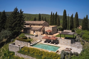 Uma villa de pedra com piscina, área de estar ao ar livre e vista para as colinas ao redor.