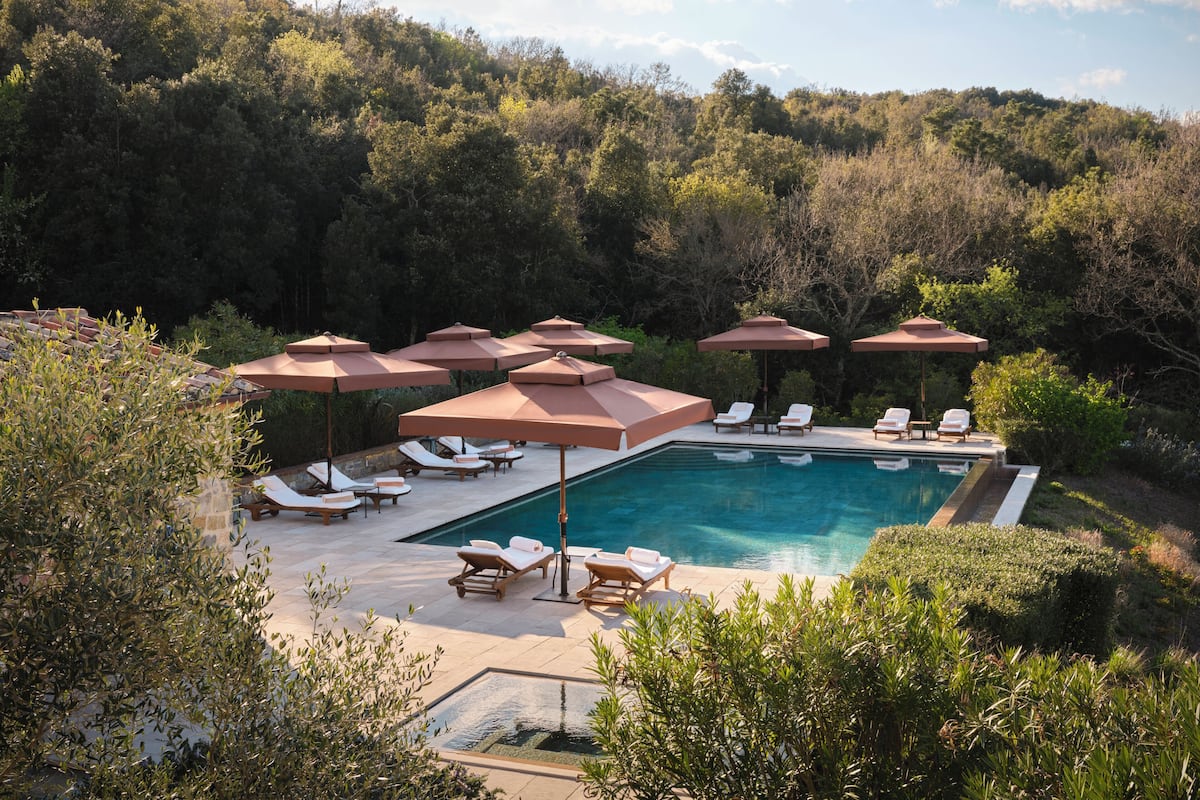 Piscina com espreguiçadeiras e guarda-sóis, rodeada por vegetação exuberante.