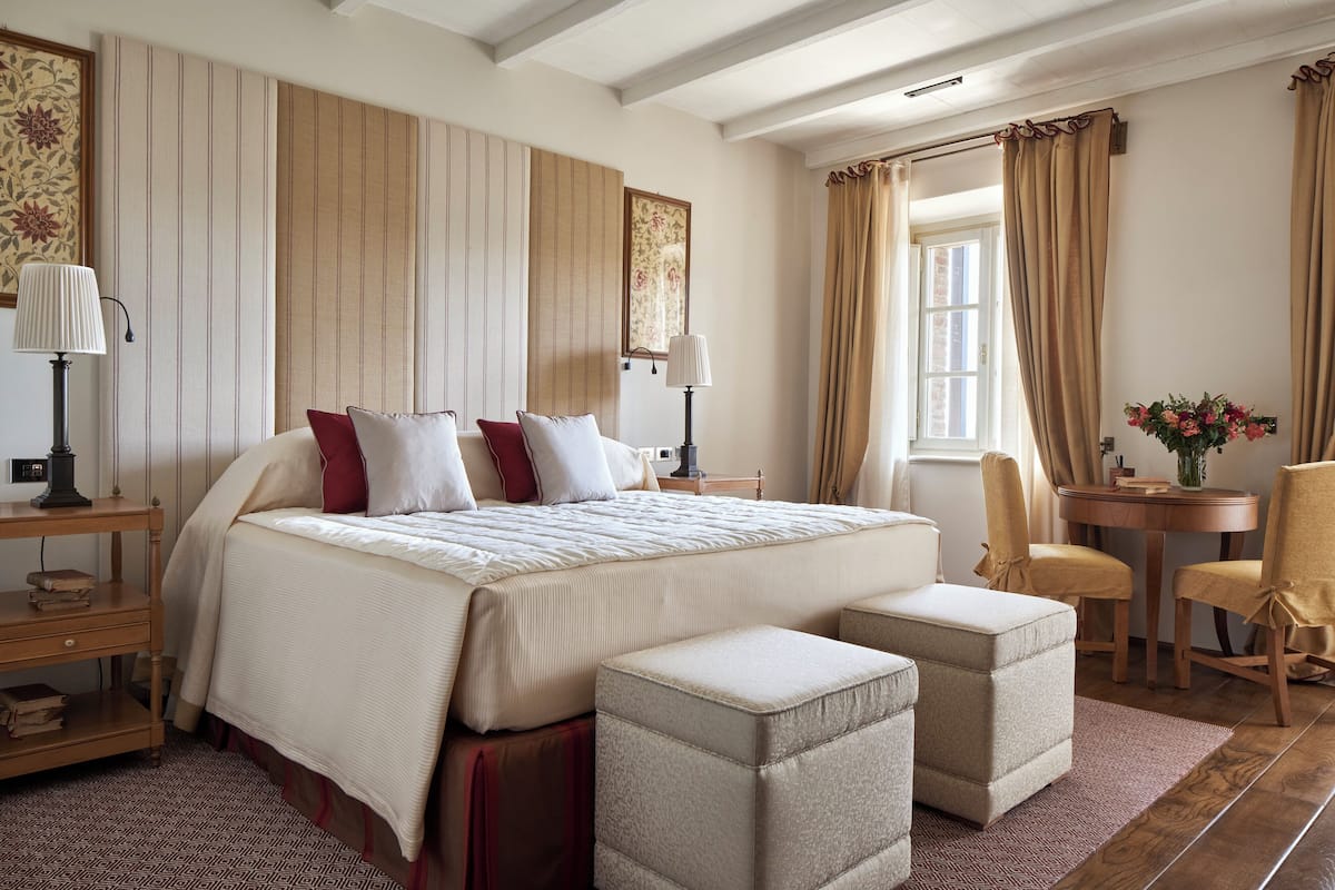 Quarto de hotel bem arrumado com uma cama grande, duas mesas de cabeceira, uma mesinha redonda e uma cadeira.