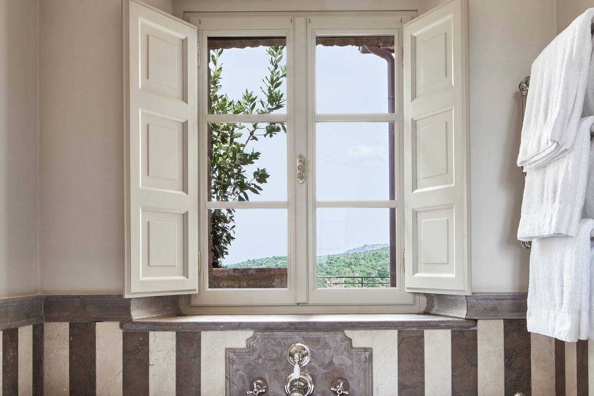 Casa de banho com uma banheira grande, uma janela com as persianas abertas e um porta-toalhas.
