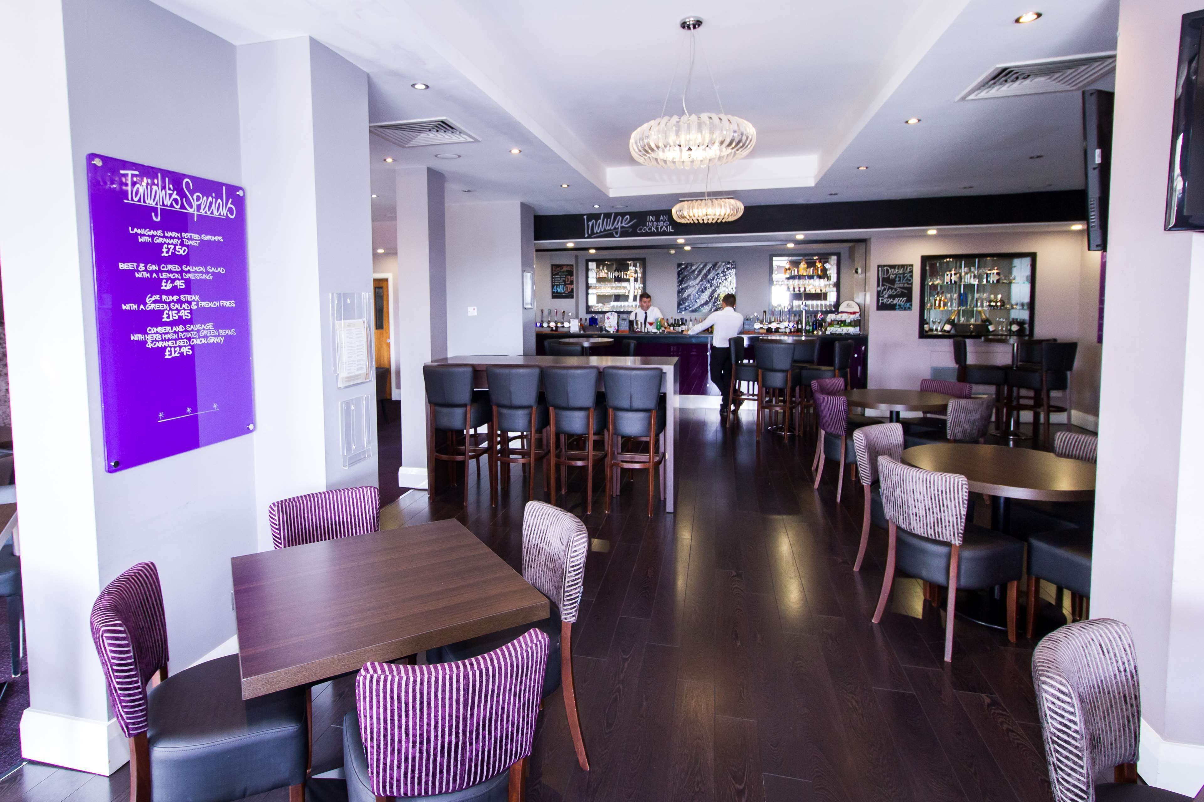 Um restaurante com área de bar, diversos arranjos de mesas e um quadro de cardápio na parede.