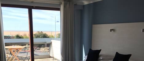Quarto de hotel com uma cama grande, vista para a praia e varanda com móveis de exterior.