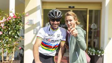 Uma pessoa com jersey de ciclismo e capacete em frente à entrada de um edifício.
