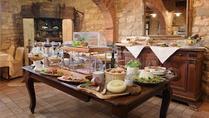 Disposição de buffet em um espaço rústico com paredes de pedra, mesa de madeira, diversos alimentos e um espelho na parede.