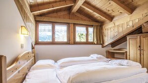 Quarto com duas camas, vigas de madeira, janela com cortinas e um armário de madeira.
