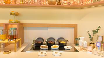 Buffet de café da manhã com diversas opções de alimentos, um espaço para café e um dispensador de sucos.