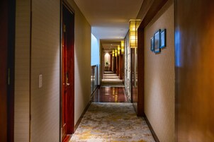 Corredor de hotel com paredes de madeira, piso de mármore e luminárias fixadas na parede.