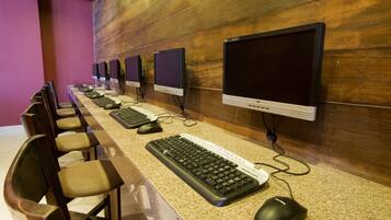 Uma fileira de computadores com monitores, teclados e mouses, em frente a uma parede de madeira.