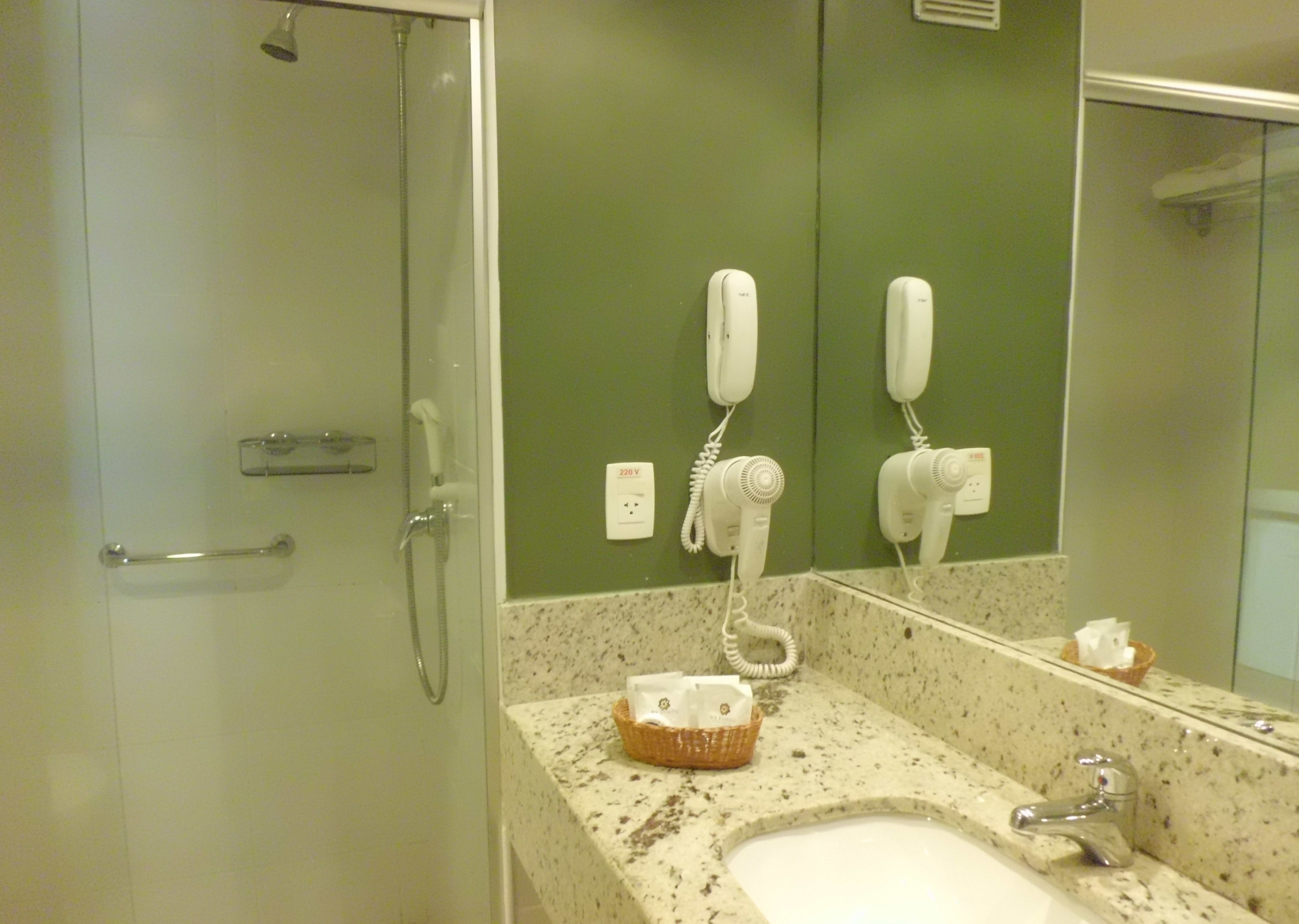 Casa de banho com lavatório, espelho, secador de cabelo e chuveiro.
