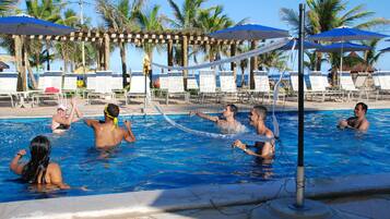 Área de piscina com espreguiçadeiras e guarda-sóis, cercada por palmeiras.