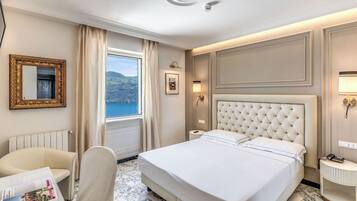 Quarto de hotel com uma cama grande, uma cadeira, uma mesa com uma revista, uma janela com vista e um espelho.
