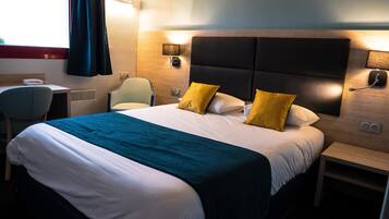Quarto de hotel com uma cama grande, duas mesas de cabeceira, uma escrivaninha, uma cadeira e uma janela com cortinas.