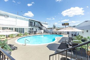Piscina com espreguiçadeiras e guarda-sóis, um edifício com escadaria e uma antena parabólica.