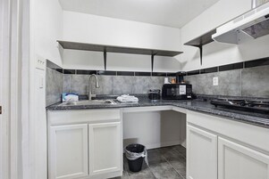 Cozinha moderna com armários brancos, bancada de granito, coifa de aço inoxidável, micro-ondas e lixeira.