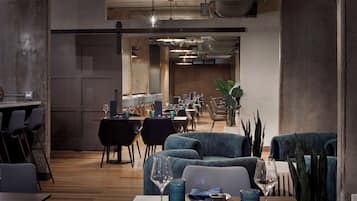 Interior moderno de restaurante com piso de madeira, assentos estofados em azul e uma extensa área de jantar com mesas e cadeiras.