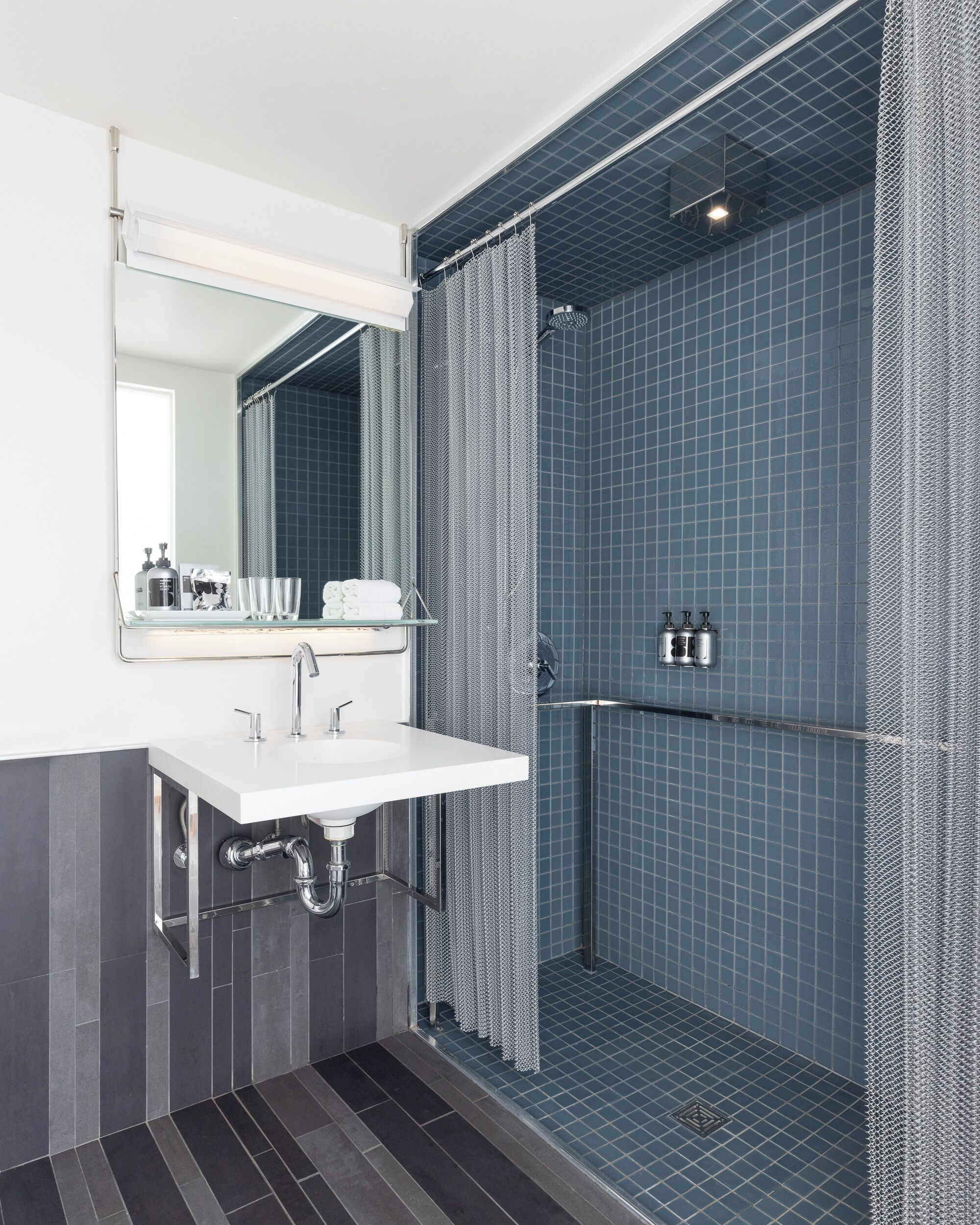 Uma casa de banho moderna com lavatório branco, espelho e zona de duche com azulejos azuis.