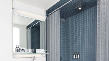 Uma casa de banho moderna com lavatório branco, espelho e zona de duche com azulejos azuis.