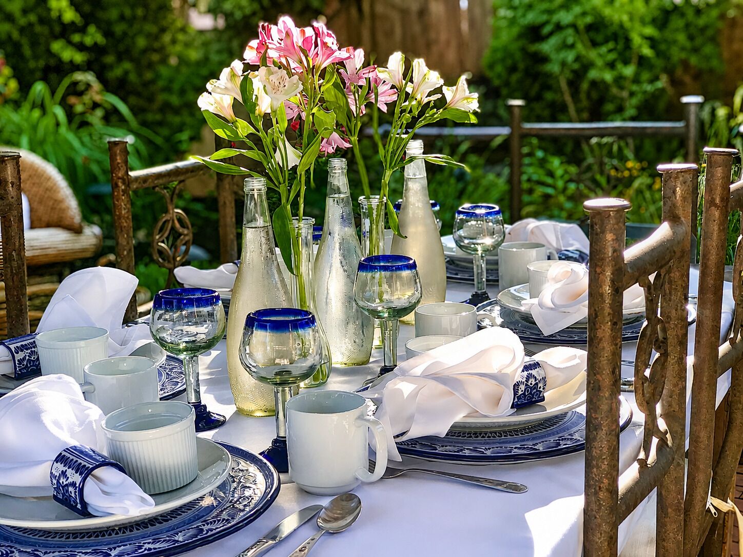 Uma mesa posta com louças azul e branco, garrafas de vidro transparente e um vaso com flores.