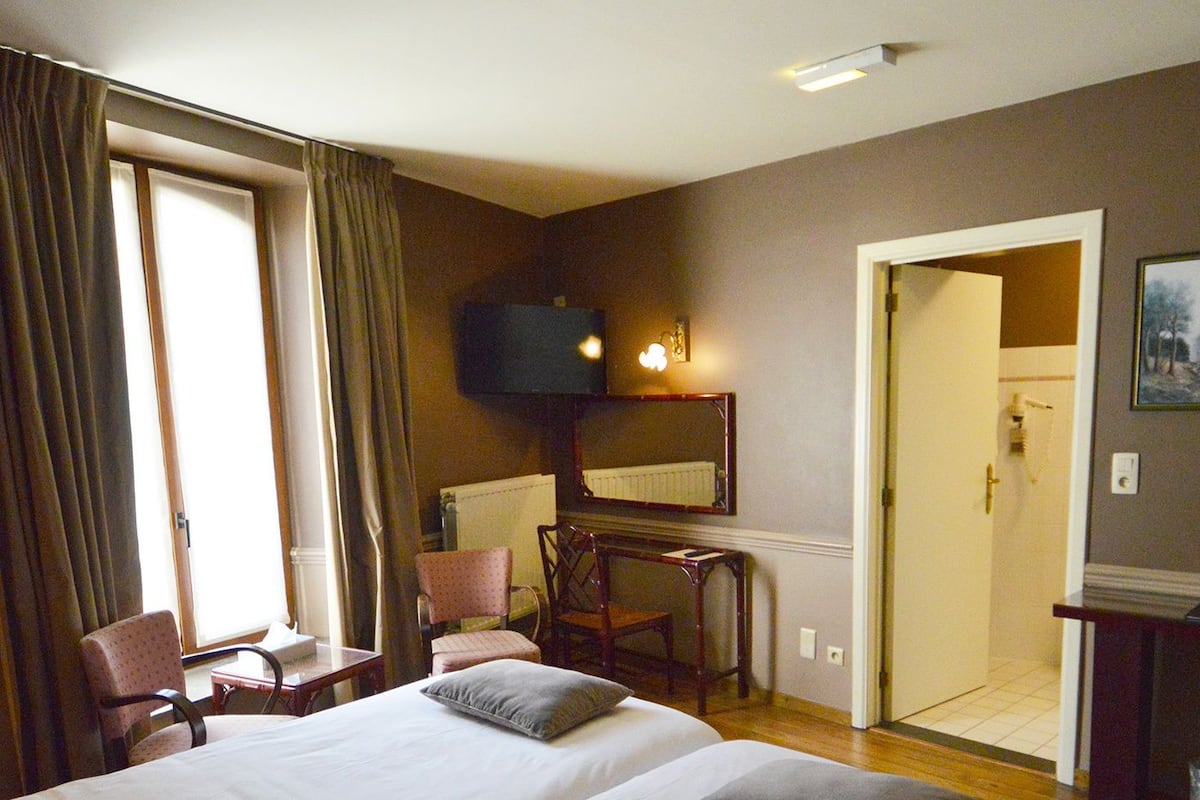 Quarto de hotel com duas camas, uma escrivaninha, uma cadeira, uma televisão e uma porta que dá para o banheiro.