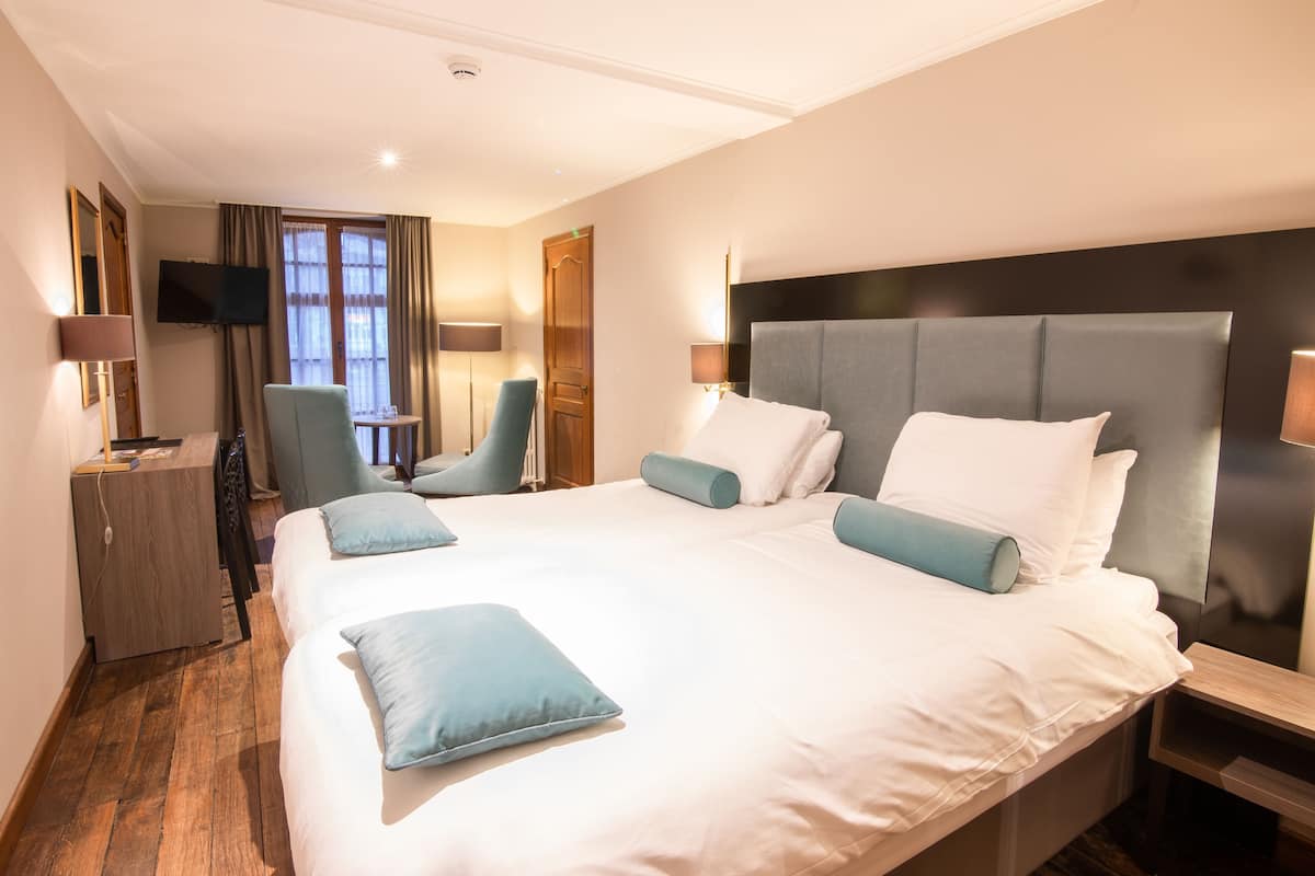 Quarto de hotel com uma cama grande, duas poltronas, uma escrivaninha e uma televisão.