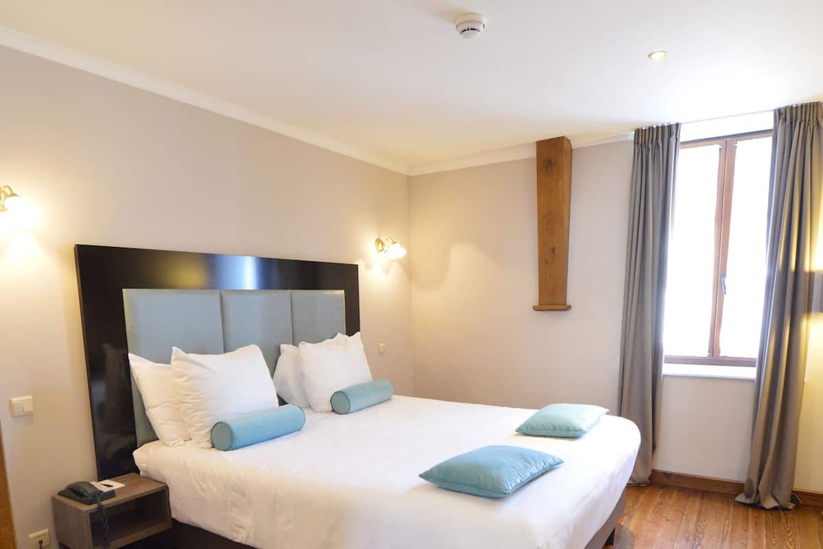 Uma cama grande com cabeceira, mesas de cabeceira e uma janela com cortinas.