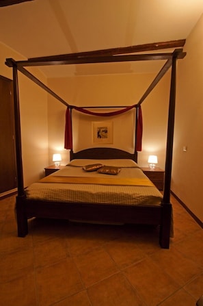 Uma cama com dossel, duas mesas de cabeceira com abajures, e um quadro pendurado na parede.