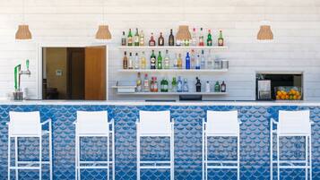Uma área de bar com painel de azulejos azuis, banquetas brancas e prateleiras repletas de garrafas diversas.