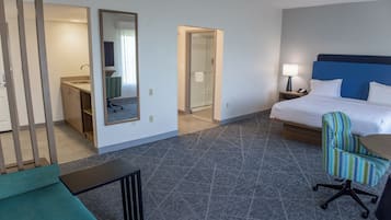 Quarto de hotel com cama, escrivaninha, cadeira, espelho e porta do banheiro.
