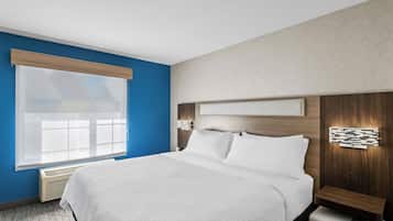 Quarto de hotel com uma cama grande, janela com persianas, luminária fixada na parede e cabeceira de madeira.