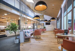 Amplo espaço interior com piso de madeira, diversos assentos e grandes janelas que permitem entrada de luz natural.
