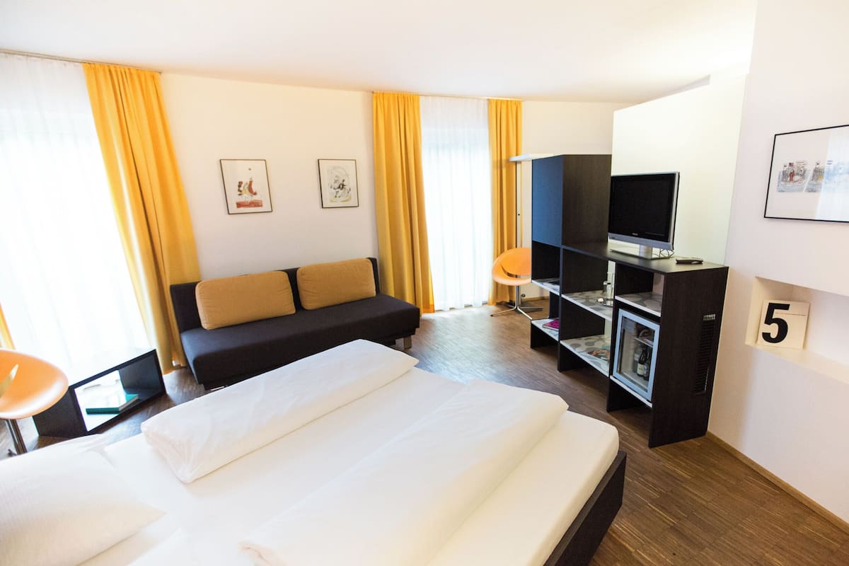 Quarto de hotel com cama, sofá, televisão e minibar.