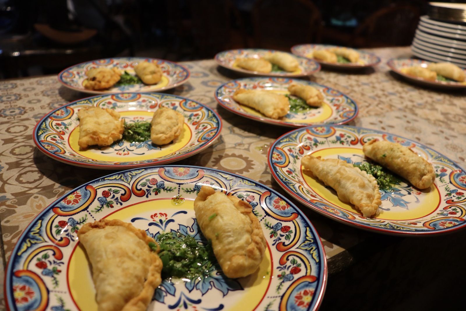 Uma mesa com pratos de pastelaria e uma pilha de pratos ao fundo.