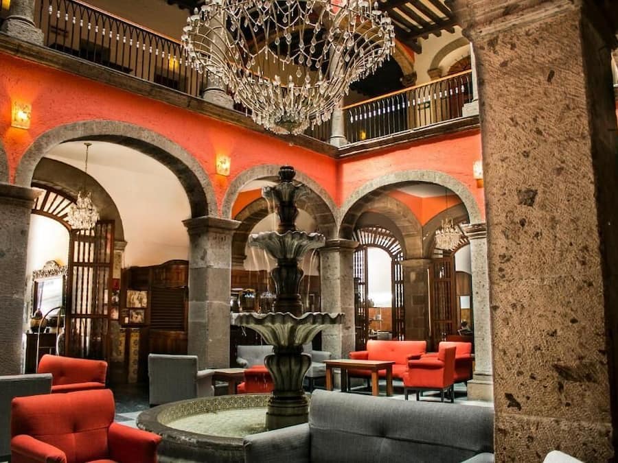 Um hall com uma fonte, assentos em vermelho e cinza, e um candelabro.
