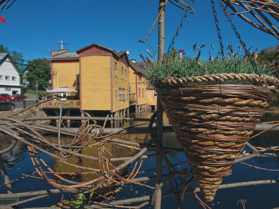 Um edifício amarelo com telhado vermelho, um cais de madeira e uma cesta de vime com plantas.