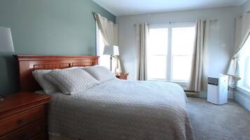 Uma cama bem arrumada com cabeceira de madeira, mesa de cabeceira com abajur e janela com cortinas.