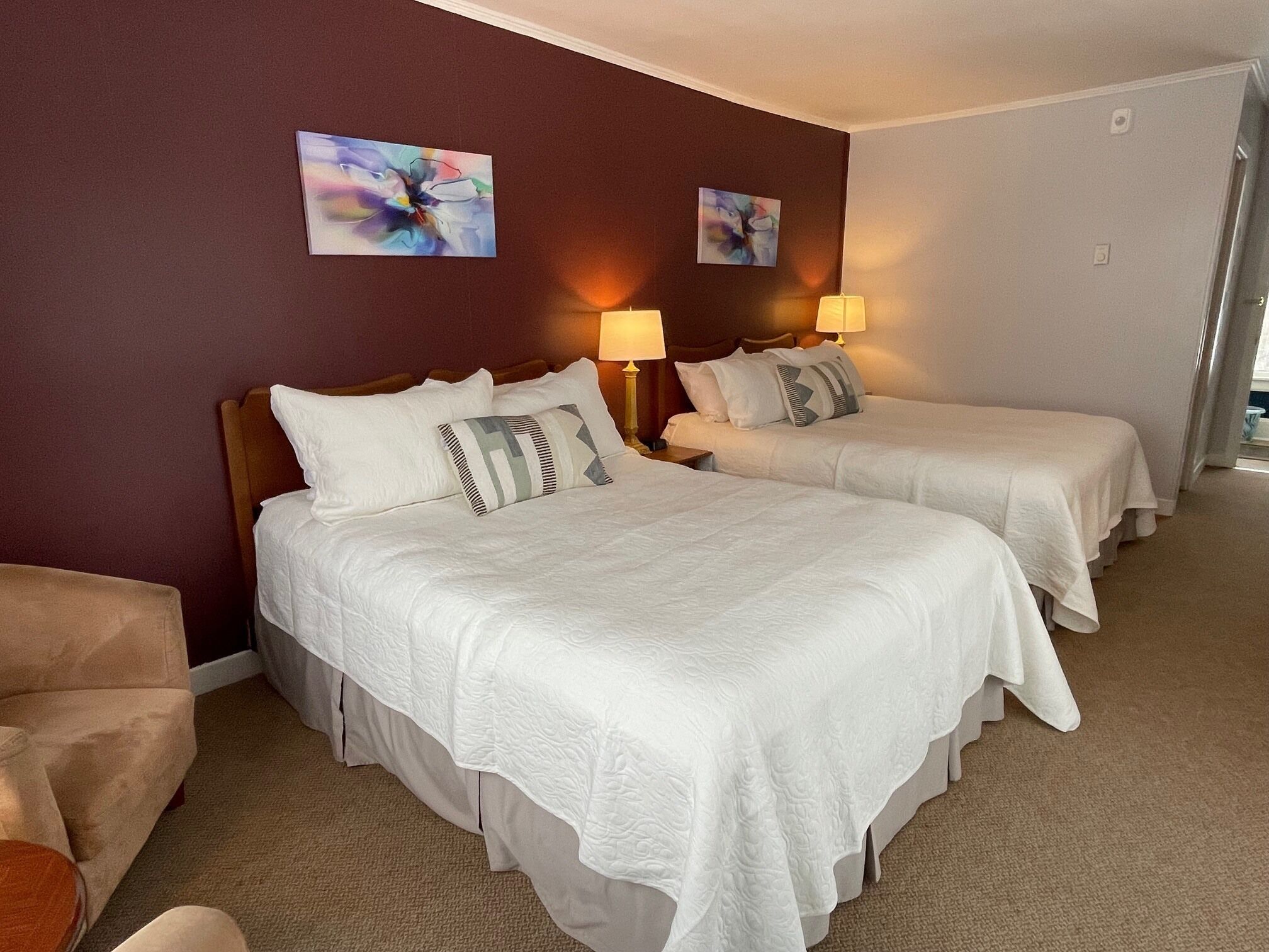 Quarto de hotel com duas camas, um sofá e duas luminárias fixadas na parede.