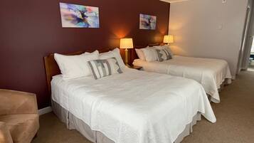 Quarto de hotel com duas camas, um sofá e duas luminárias fixadas na parede.