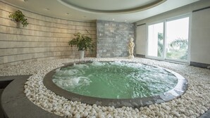 Área de spa com hidromassagem, cercada por pedras, uma parede de pedra e uma estátua.