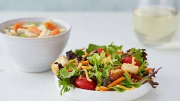 Uma tigela de sopa e uma salada com croutons e queijo em um prato branco.